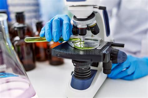 Young Blond Man Scientist Using Microscope Pouring Liquid On Sample At Laboratory Stock Image
