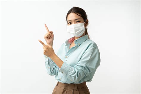 젊은 행복한 아시아 여성은 흰색 배경에 고립 된 코로나 바이러스 감염 촬영을 방지하기 위해 위생 마스크를 착용 공간을 복사하기 위해 손가락 손을 가리키는 파란색 셔츠를