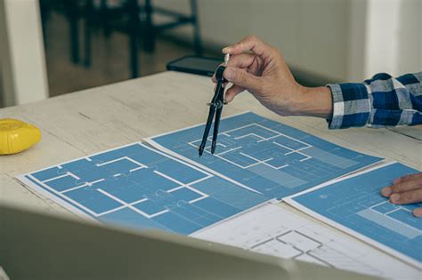 젊은 엔지니어와 건축가는 모자와 주택이 있는 시공 개념의 탁상 도구로 청사진의 레이아웃을 설계 계획 측정합니다