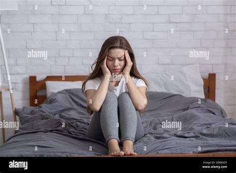 Unhappy Millennial Lady Sitting On Bed And Massaging Her Temples