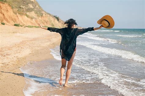 바다 파도에서 모래 해변에서 걷고 휴식을 취하는 모자를 쓴 아름다운 평온한 여성 여름 방학 밝은 검은 셔츠와 열대 섬에서 휴가를