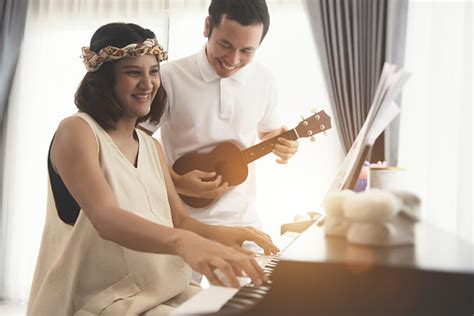 임신 한 사랑에 커플 행복 임신 한 부부는 자연 따뜻한 빛과 집에서 피아노와 우쿨렐레를 연주합니다 임신 한 부부의 관계에 대한 낭만적 인 순간 아기를 기다리는 시간 희망의