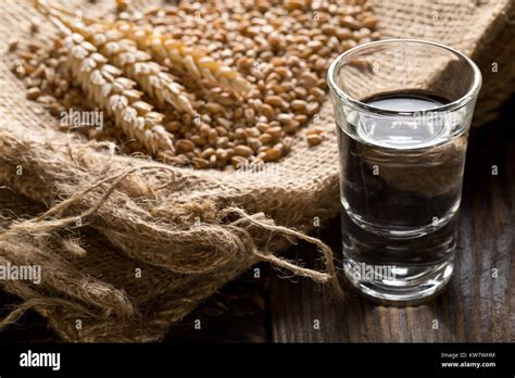 German Hard Liquor Korn Schnapps In Shot Glass With Wheat Grains And Ears On Burlap Sack On