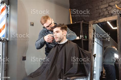 마스터는 이발소에서 남자의 머리와 수염을 잘라 미용사는 젊은 남자를위한 헤어 스타일을만든다 이발소에서 클리퍼 기계와 이발사 작업