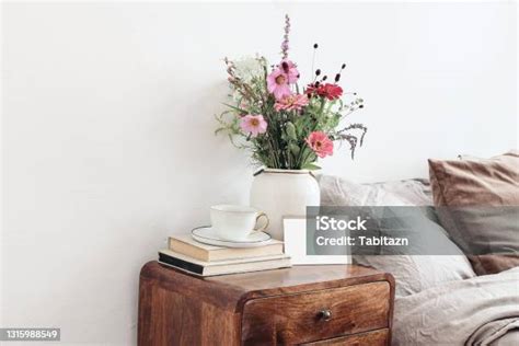 복고풍 나무 침대 옆 테이블에 커피와 책 한 잔 빈 인사말 카드 모형 흰색 세라믹 화병 우주와 진니아 꽃의 부케 베이지 색 린넨