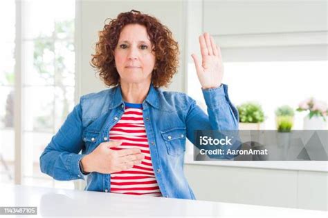 가슴 및 열려있는 손바닥에 손으로 맹세에서 데님 재킷을 입고 곱슬 머리를 가진 중간 나이 고위 여자 충성 약속 맹세 만들기 가정 생활에 대한 스톡 사진 및 기타 이미지