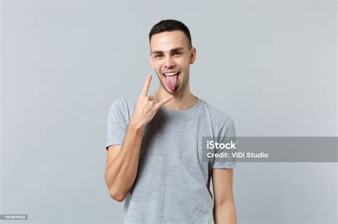 혀를 보여주는 캐주얼 복장에 재미 젊은 남자 회색 배경에 고립 된 무거운 금속 바위 기호 제스처를 묘사 사람들은 진심으로 감정 라이프 스타일 개념입니다 복사 공간을 모의