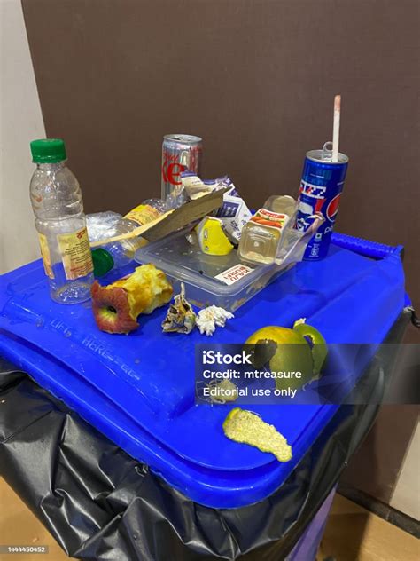 쓰레기로 덮인 파란색 플라스틱 바퀴 달린 쓰레기통의 닫힌 뚜껑 쓰레기통을 감싸는 검은 쓰레기 봉투 일회용 용기 일회용 플라스틱