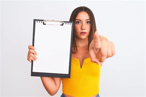 카메라와 당신에 게 손가락으로 가리키는 고립 된 흰색 배경 위에 서 클립 보드를 들고 젊은 아름 다운 소녀 손 기호 앞에서 긍정적이 고 자신감 제스처 가리키기에 대한 스톡