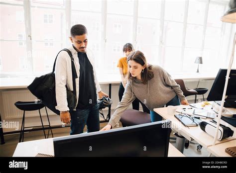 Female Programmer Showing Computer To Coworkers Against Window In