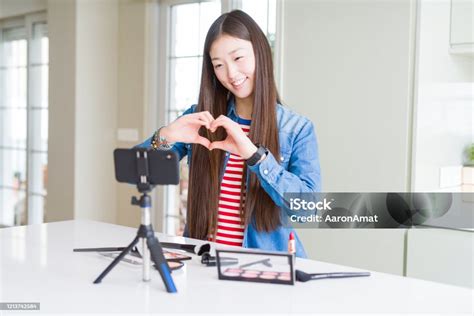 아름 다운 아시아 영향력 여자 기록 메이크업 자습서 스마트폰 카메라를 사용 하 여 미소 사랑에 심장 기호와 손으로 모양을