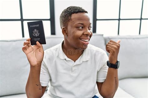Young African Man Holding United States Passport Pointing Thumb Up To The Side Smiling Happy