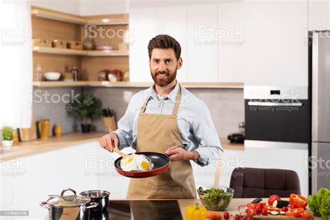 앞치마를 입은 웃는 성인 유럽 수염 난 남자 요리사는 현대적인 주방 인테리어에서 스크램블 에그를 준비합니다 남자에 대한 스톡 사진 및 기타 이미지 Istock