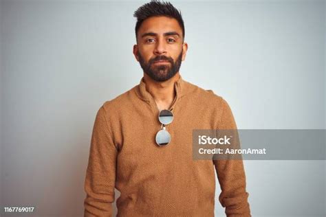 우아한 스웨터와 선글라스를 입고 고립 된 흰색 배경 위에 서있는 인도 남자얼굴에 심각한 표정 카메라를 보는 간단하고 자연스러운 겨울에 대한 스톡 사진 및 기타 이미지