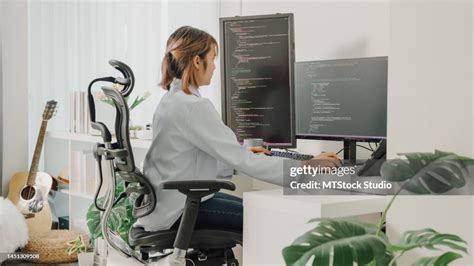 Young Asian Woman Software Developers Using Computer To Write Code Sitting At Desk With Multiple