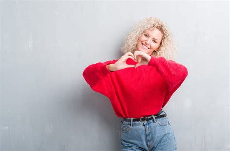 그런 지 회색 배경에 마음 기호와 손으로 모양을 보여주는 사랑에 웃 고 곱슬 머리를 가진 젊은 금발 여자 낭만적인 개념입니다 개념에 대한 스톡 사진 및 기타 이미지 Istock