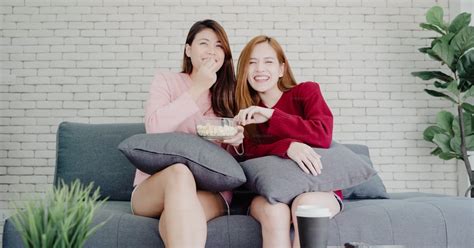 레즈비언 아시아 커플은 집에서 거실에서 Tv를 보고 팝콘을 먹고 달콤한 커플은 집에서 휴식을 취할 때 소파에 누워 재미있는 순간을 즐깁니다 라이프스타일 커플은 집에서
