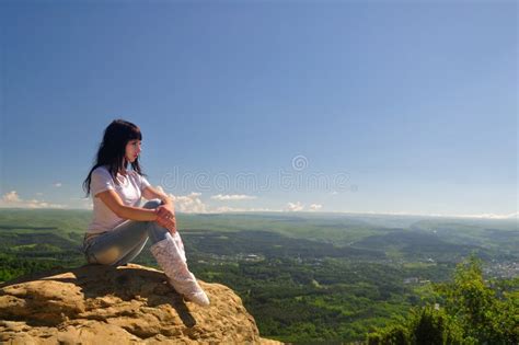 Девушка сидит на краю скалы и смотреть в расстояние Стоковое Изображение изображение