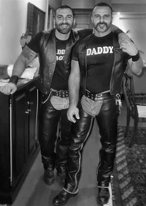 Two Men Standing Next To Each Other Wearing Leather Pants And Boots