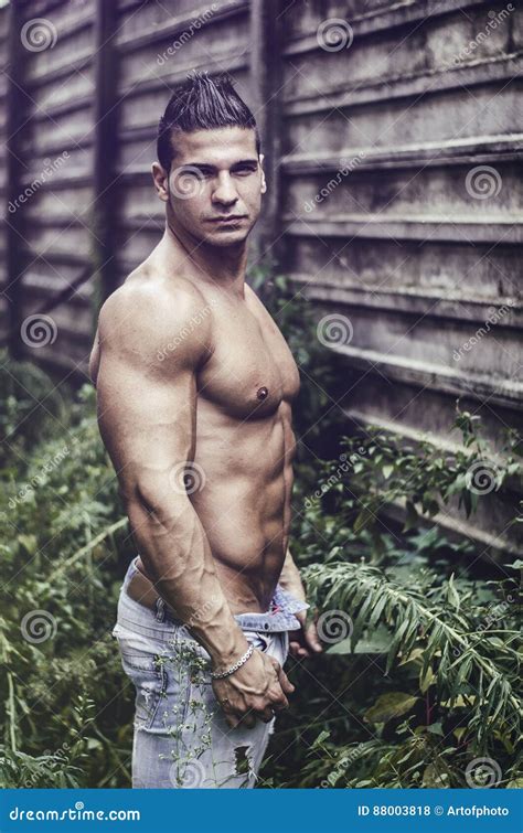 Muscular Young Latino Man Shirtless In Jeans In Front Of Concrete Wall