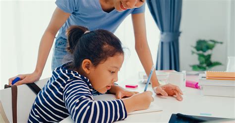 스웨터를 입은 아시아 유아 소녀는 메모장이 있는 책상 앞에 앉아 연필을 사용하여 공책 쓰기에 집중하고 주말에 집에서 어머니나 가정교사와 함께 수학 숙제를 합니다 원격 온라인