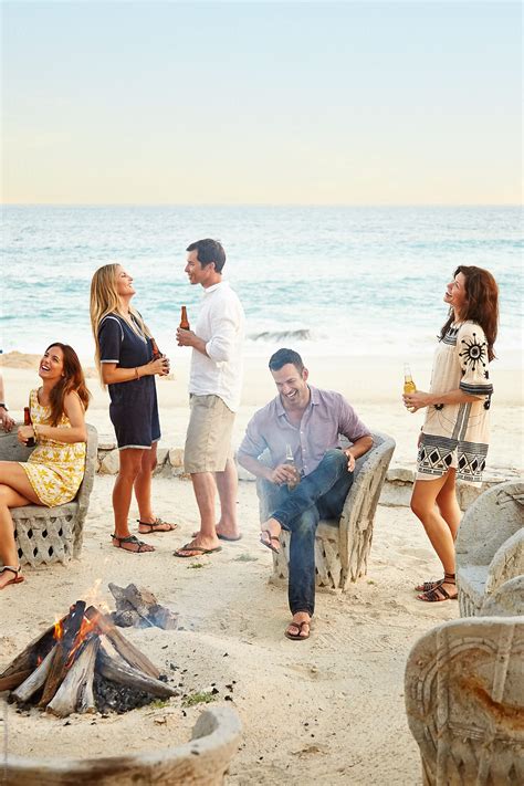 Friends Drinking Beers Around A Fire Pit On The Beach By Stocksy
