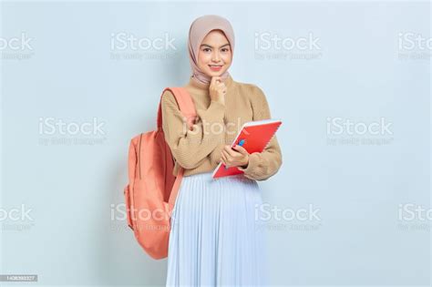 배낭으로 갈색 스웨터를 입은 젊은 아시아 무슬림 여성 학생을 웃고 책을 들고 흰색 배경에 고립 된 것에 대해 생각합니다 학교 개념으로 돌아가기 20 24세에 대한 스톡 사진