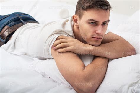 Фотография на тему Парень в белой футболке и синих джинсах лежит на кровати Pressfoto