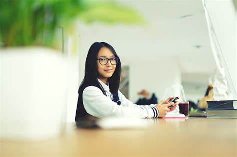 스마트폰 4g 무료 인터넷 연결을 사용 하 여 친구와 채팅 하는 웃는 중국 학생의 초상화 도서관에서 공부 하 고 카메라에 안경에 행복 한 아름 다운 젊은 아시아