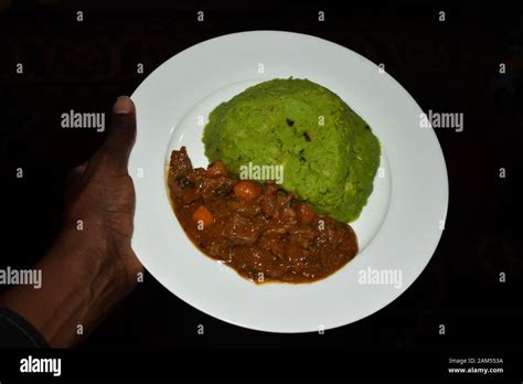 A Hand Holding Up A Plate Of Kenyan Traditional Dish Called Mukimo In A Dark Setting Dish Is