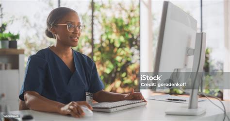 일상적인 병원 운영을 위해 데스크톱 컴퓨터를 사용하는 아프리카 의료 간호사 공공 의료 시설의 현대 사무실에서 온라인 의료 작업을 위해 Pc를 사용하는 아름다운 젊은 클리닉