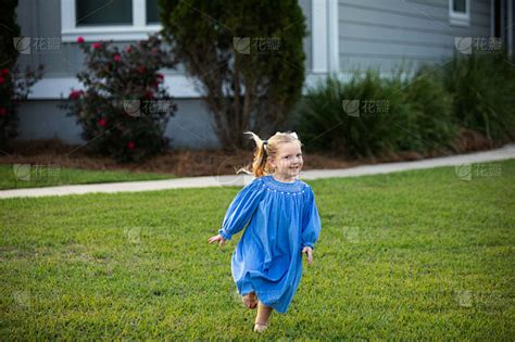 小女孩扎着辫子，穿着蓝色的裙子，在一所新建筑房子的草坪上奔跑