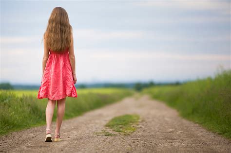 푸른 하늘 복사 공간 배경에 화창한 여름 날에 녹색 필드를 따라 지상 도로를 걷는 긴 머리와 빨간 드레스에 젊은 낭만적 인 슬림 여성의 백보기 계절에 대한 스톡 사진 및