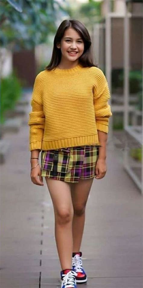 A Woman In Yellow Sweater And Plaid Skirt Walking Down The Street With