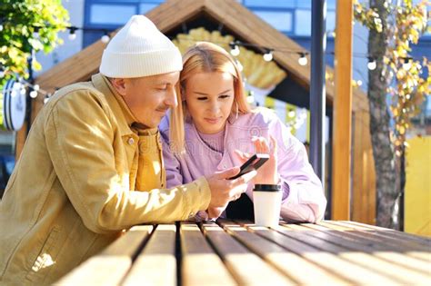 A Young Man And His Girlfriend Are Sitting At The Wooden Table Of A