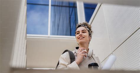 한 여성 젊은 성인 백인 여학생이 배낭을 메고 대학 건물 앞에 서서 종이와 커피 한 잔을 들고 밝은 날에 야외에서 행복한 미소를 지으며 실제 사람들이 공간을 복사한다 사진