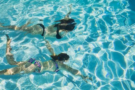 Two Girls Are Swimming Underwater In A Pool With Shiny Water Stock