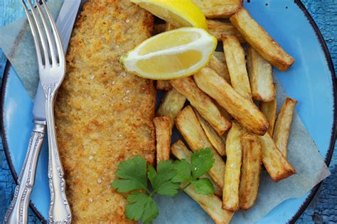 기름진 양피지 칼과 포크 레몬 슬라이스 청록색 나무 곡물 배경 높은 전망과 청록색 접시에 파슬리로 장식 된 피시 앤 칩스 의