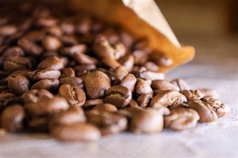 향긋하게 볶은 커피 원두를 열린 크래프트 종이 봉지에서 가벼운 질감의 표면에 붓습니다 콩의 따뜻한 갈색 색조와 부드러운 확산