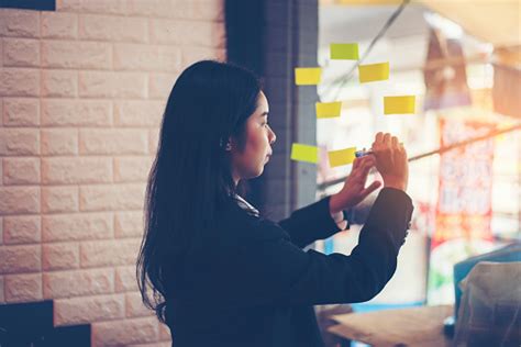 아시아 사업가는 작업 창조적 인 아이디어를 작성하고 유리 벽에 메모 끈적 끈적한 게시물에 계획을 세웁니다프로젝트 전략 계획 작성
