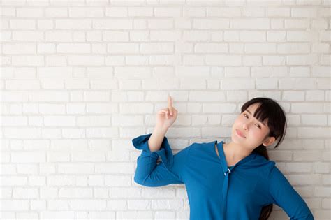 아름다운 초상화 젊은 아시아 여자는 시멘트 콘크리트 배경에 복사 공간을 가리키는 행복 소녀 서 서 웃고 미래를 보여주는 또는 당신의 메시지와 함께 계획 가리키기에 대한 스톡