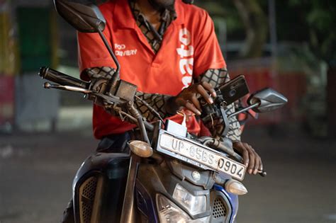 델리에서 이 식품 기술 스타트업의 성장을 보여주는 상징적인 빨간색 유니폼을 입고 길가에서 주문을 받기 위해 기다리고 있는 자전거를 탄 Zomato 라이더 배달에 대한 스톡
