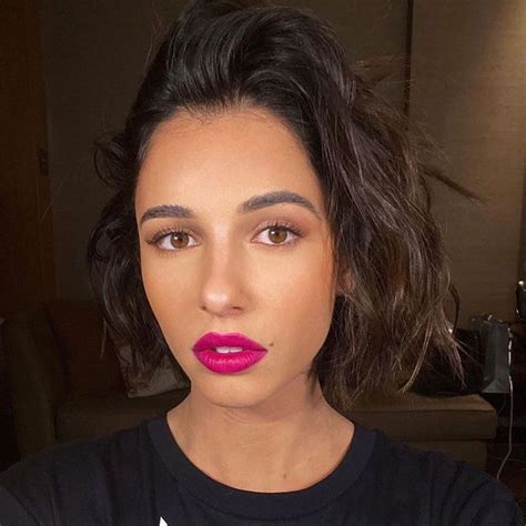 A Woman With Dark Hair And Pink Lipstick Looks At The Camera While