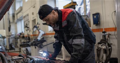 작업장에서 엔진을 부수고 수리하는 동안 열린 자동차 후드 위로 구부러진 작업복의 현대 자동차 정비사 사진 Unsplash의