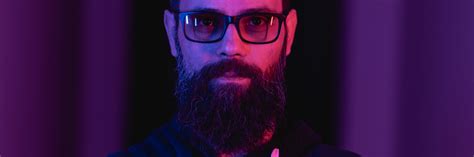 네온 조명을 가진 남자의 남성 초상화 어두운 배경의 빨강 파랑 자주색 및 자홍색 사람은 실내에서 안경 어두운 재킷을 착용합니다 여러 가지 빛깔의 빛이 있는 미래 라이프스타일