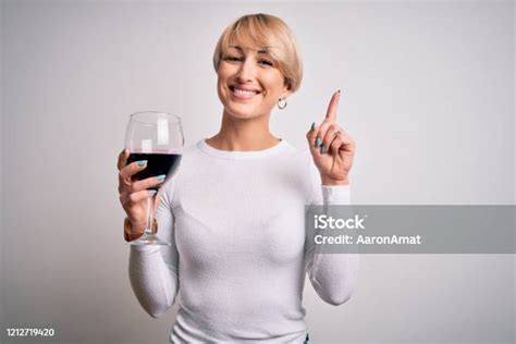 젊은 금발의 여자 와 짧은 머리 마시는 유리 한 잔 위에 고립 된 배경 놀란 와 아이디어 또는 질문 가리키는 손가락 으로 행복한 얼굴 번호 하나 가리키기에 대한 스톡 사진