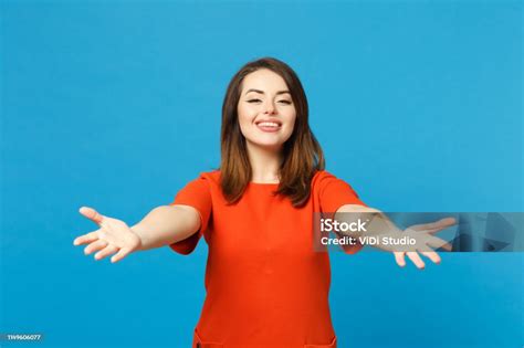 빨간 오렌지 드레스를 입고 아름 다운 젊은 여 자가 파란색 벽 배경 스튜디오 초상화에 고립 된 포즈를 서 있는 카메라에 손을 뻗어 사람들의 라이프 스타일 패션 컨셉 복사