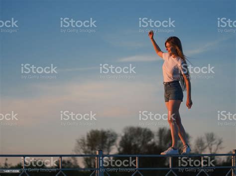 하얀 블라우스와 반바지를 입은 젊은 아름다운 여성이 균형을 유지하면서 하늘을 향해 난간을 따라 걷습니다 행복한 여름 시간 25 29세에 대한 스톡 사진 및 기타 이미지