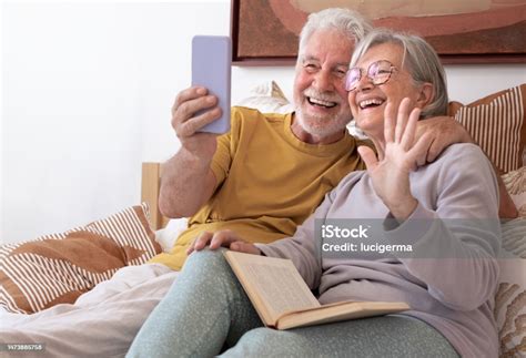 가족 및 친구들과 원격으로 의사 소통하는 노부부 침대에 앉아 스마트폰을 가진 조부모 기술 통신에 대한 개념 화상 통화에 대한