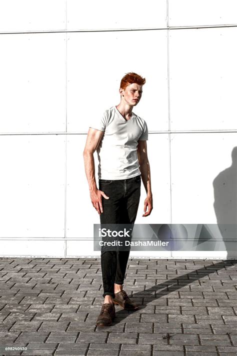 빨간 머리와 주 근 깨 흰 T 셔츠를 입고 흰색 벽 근처 서 매력적인 세련 된 젊은 남자 모델의 초상화 유행 야외 샷입니다 T